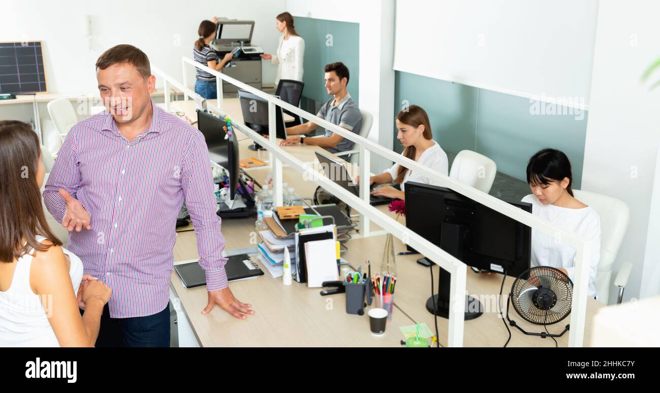Male and female office co-workers having conversation at desk in office ...