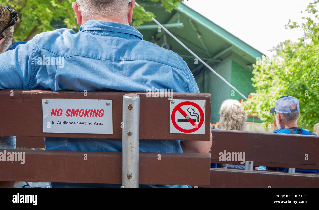 A NO SMOKING sign on the back of a wooden bench at an outdoor concert ...