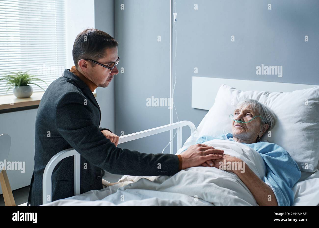 Young son supporting his senior sick mother while she lying on bed at ...
