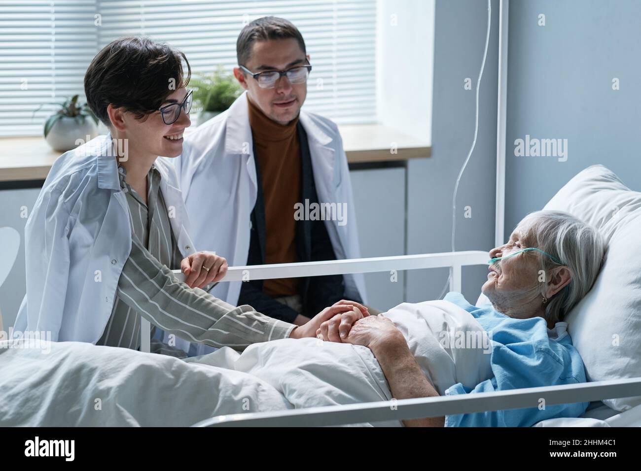 Young people supporting sick senior woman who lying on hospital bed ...