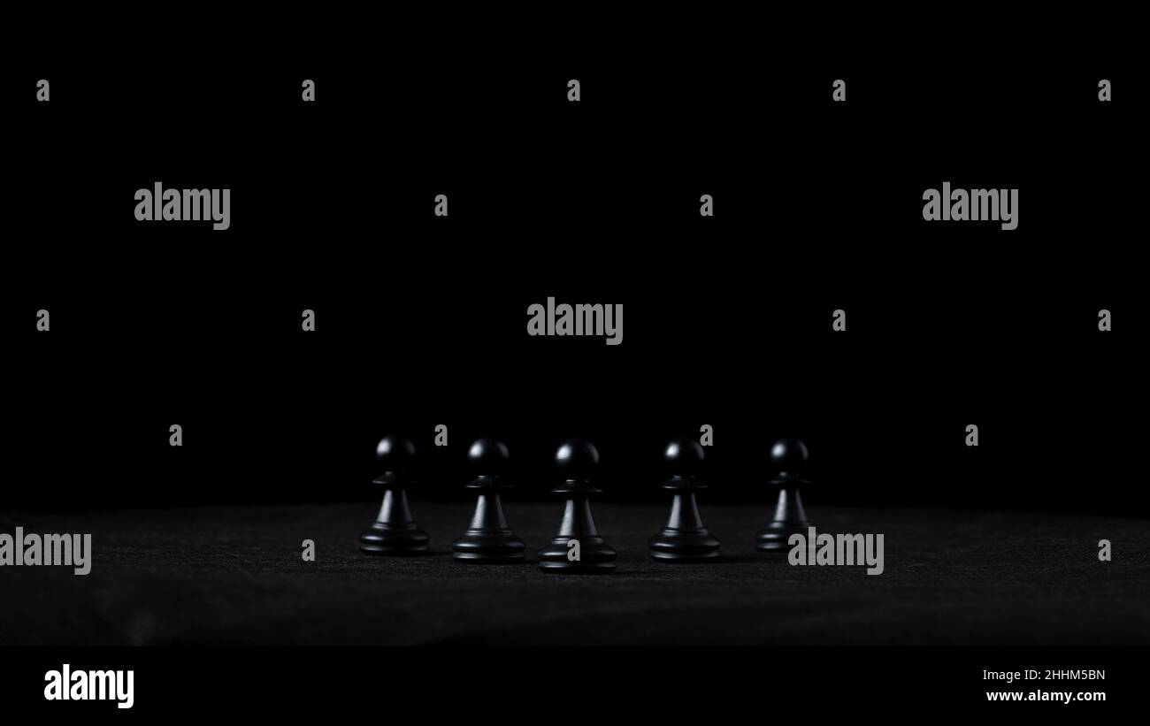 Five black pawn chess pieces placed in a row over black background in a ...