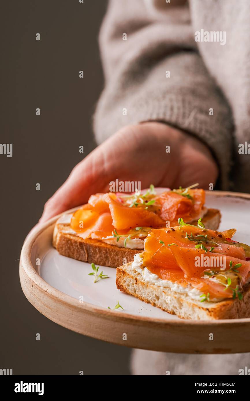 close up of woman holding white plate with smoked salmon toast as fresh ...