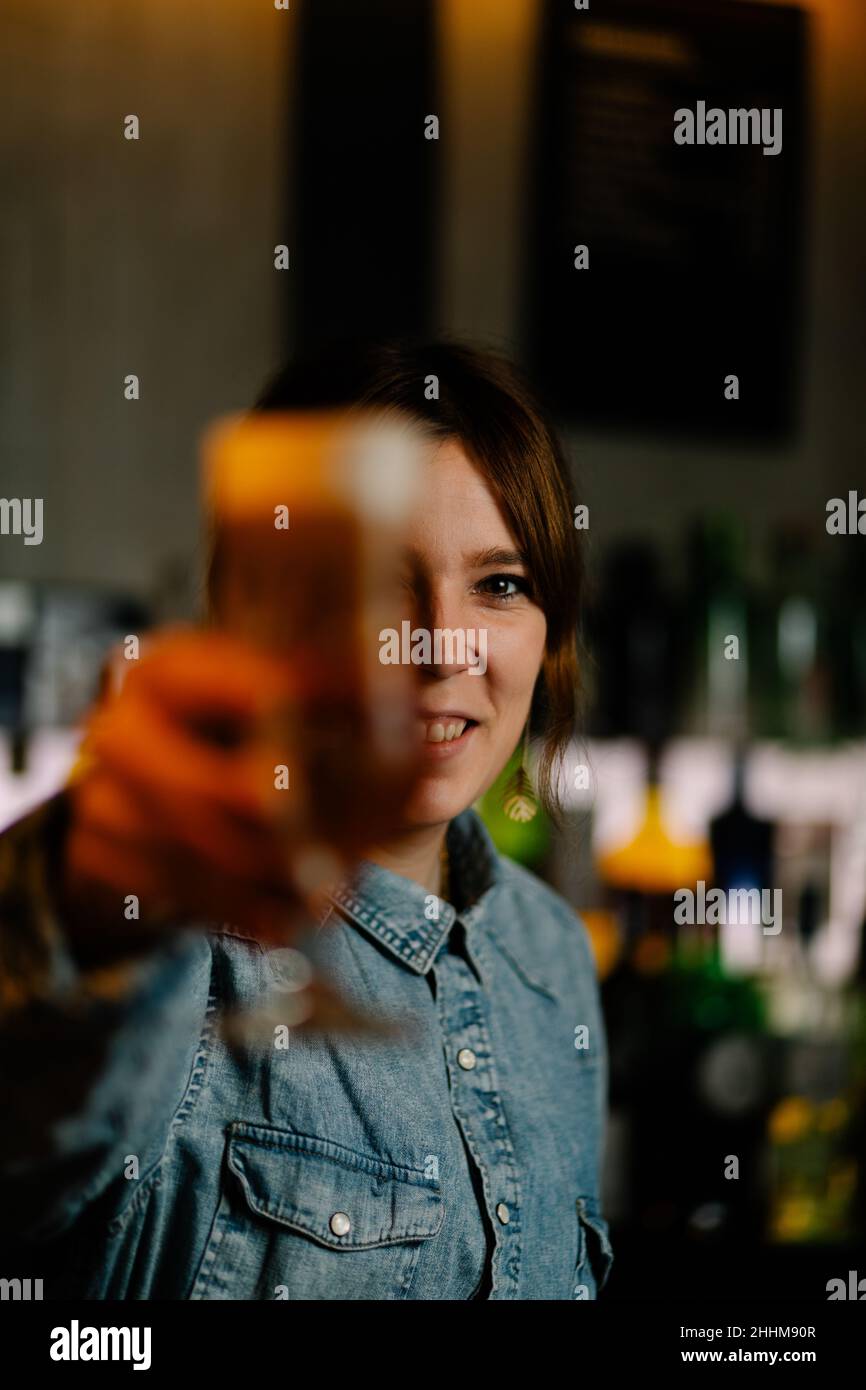 Female bartender looking at camera while serving wineglass with gin and ...
