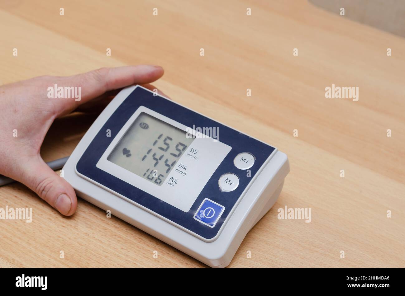 A man's hand holds a digital blood pressure monitor on the table. High ...