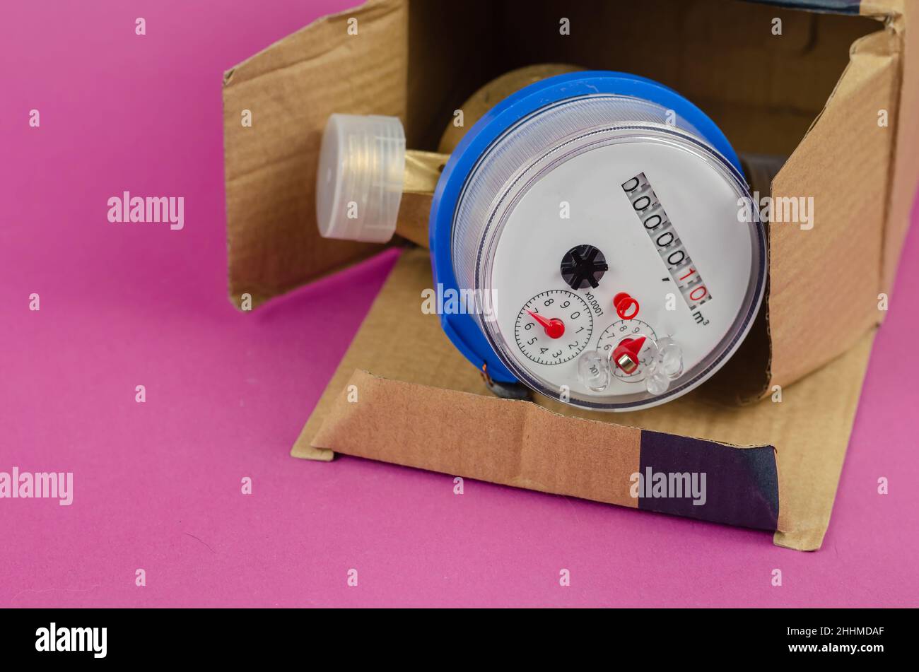 The new water meter lies in an open cardboard box against the magenta ...