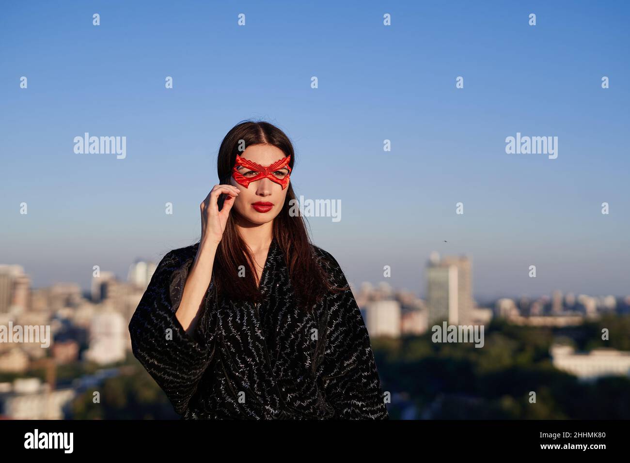 Portrait of cute brunette superhero girl in black dress and red face ...
