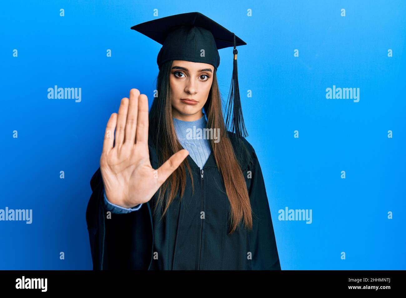 Beautiful brunette young woman wearing graduation cap and ceremony robe ...