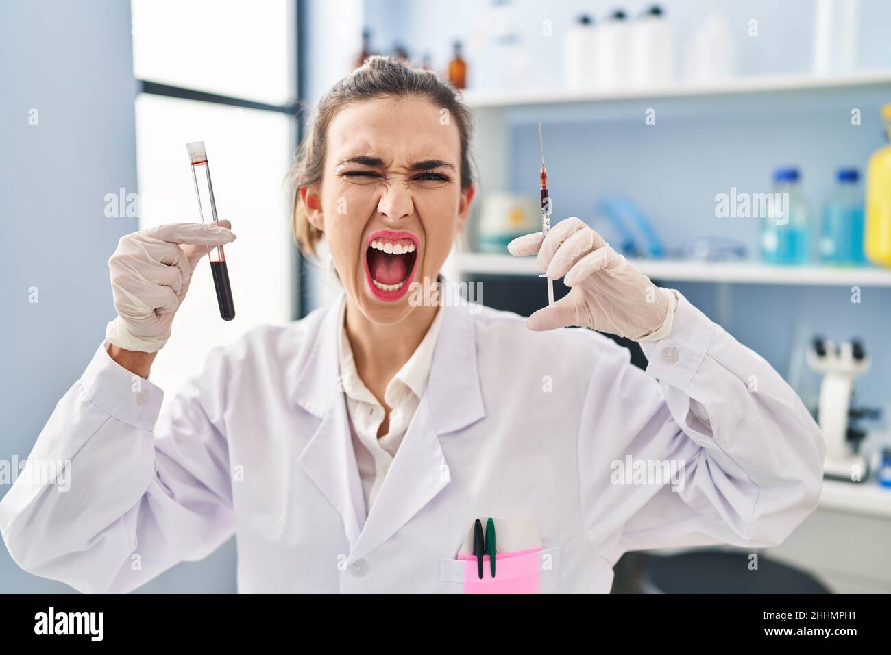 Young woman working at scientist laboratory holding blood sample angry ...