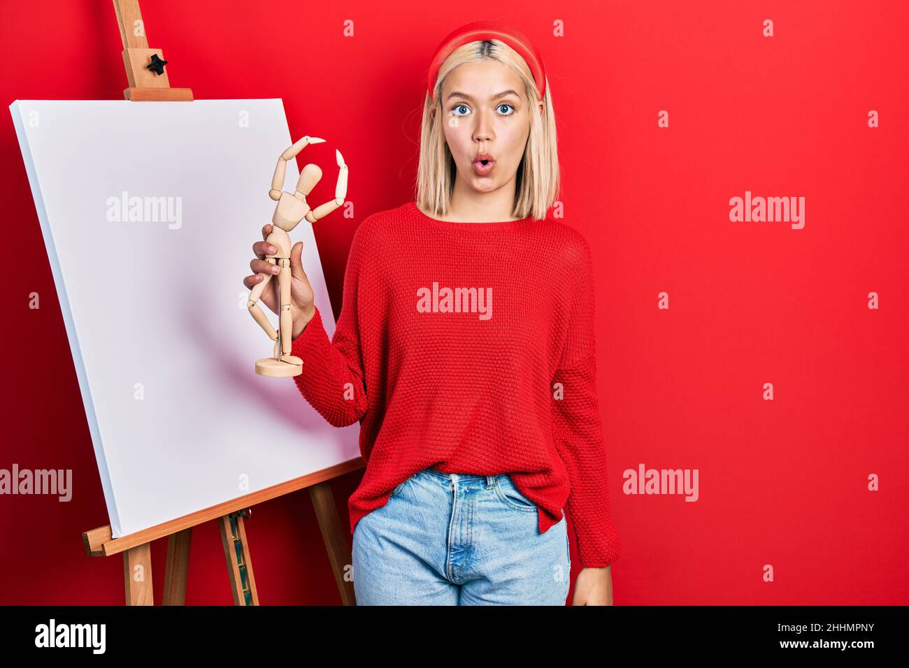 Beautiful blonde woman holding small wooden manikin scared and amazed ...