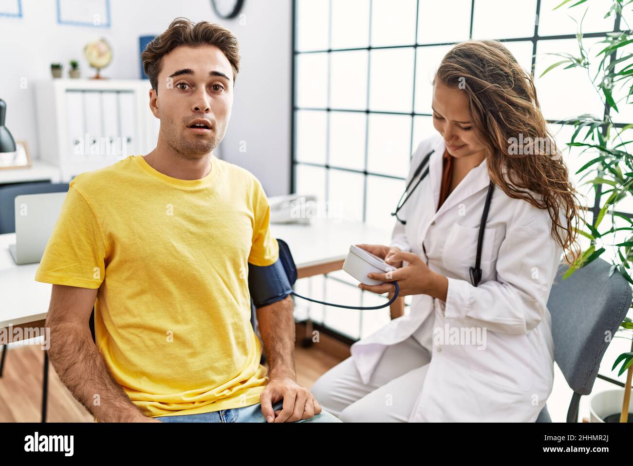 Young doctor woman checking blood pressure on patient scared and amazed ...