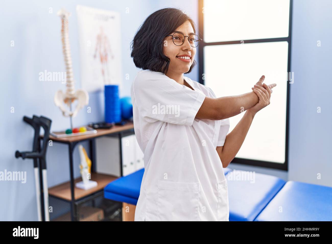 Young latin woman wearing doctor uniform stretching arms at ...