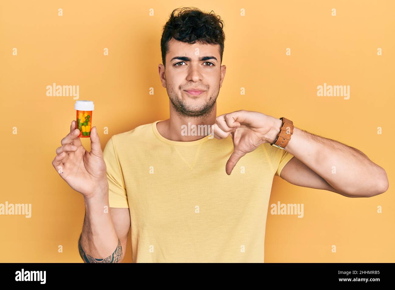 Young hispanic man holding pills with angry face, negative sign showing ...