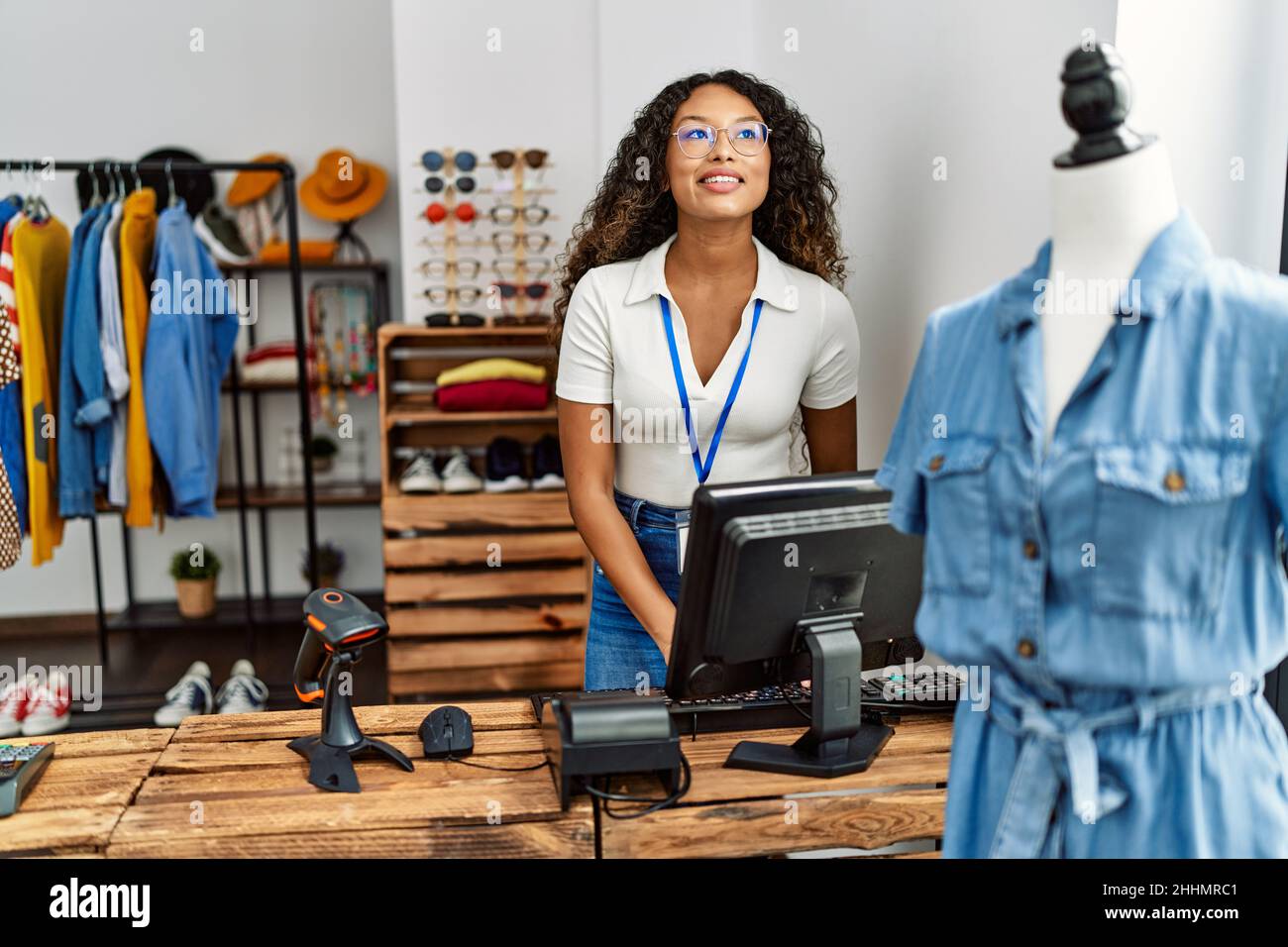 Young latin shopkeeper woman using computer working at clothing store ...