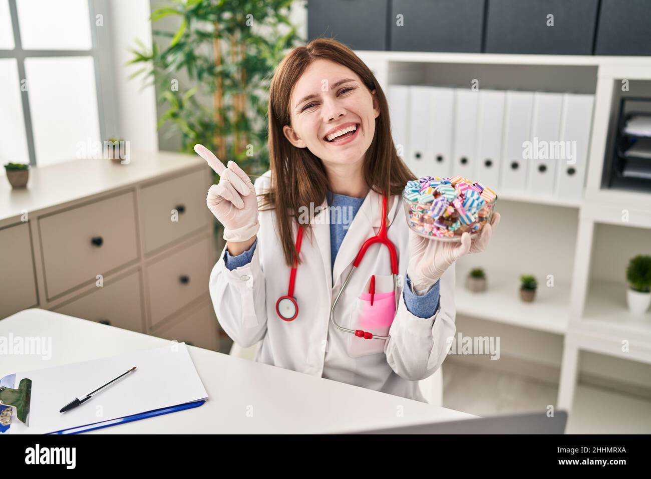 Young doctor woman holding sweets candy smiling happy pointing with ...