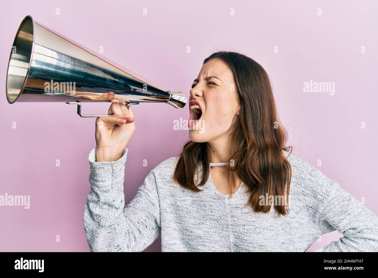 Young brunette woman shouting and screaming through vintage megaphone ...