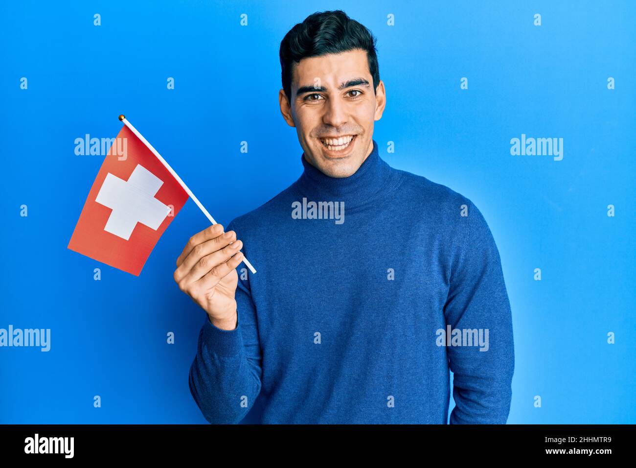 Handsome hispanic man holding switzerland flag looking positive and ...