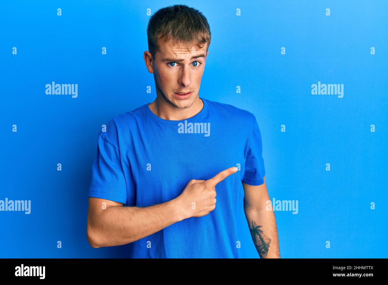 Young caucasian man wearing casual blue t shirt pointing aside worried ...