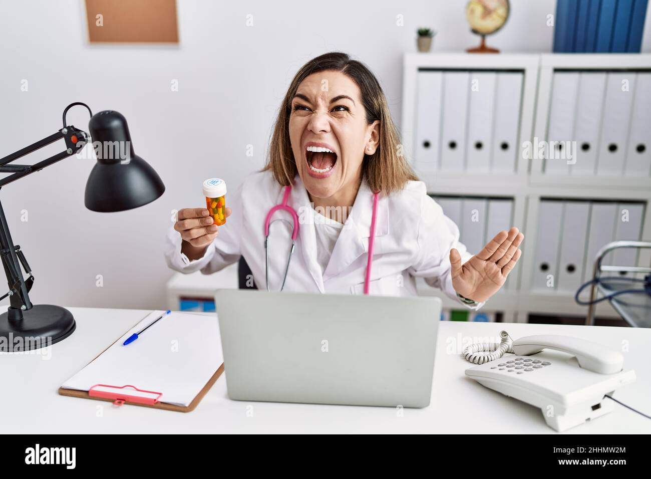 Young hispanic woman wearing doctor uniform holding pills at the clinic ...