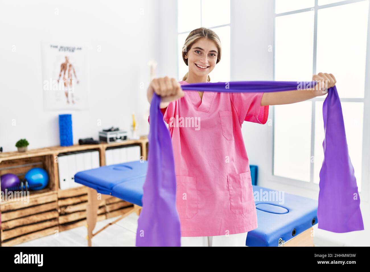 Young caucasian woman wearing physiotherapist uniform using elastica ...