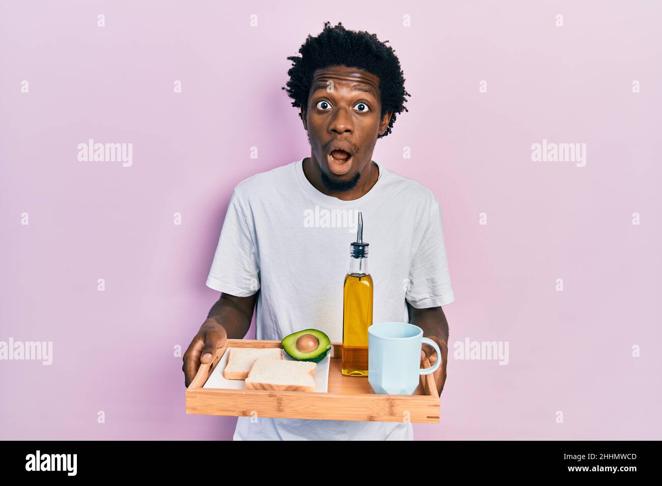 Young african american man holding tray with breakfast food afraid and shocked with surprise and ...