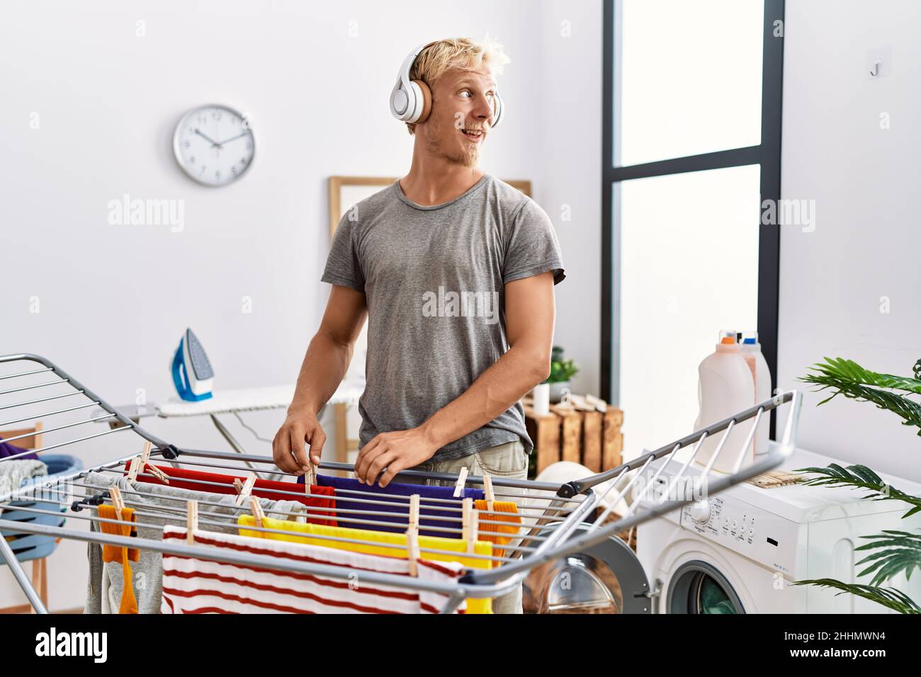 Young caucasian man listening to music hanging clothes at laundry room ...