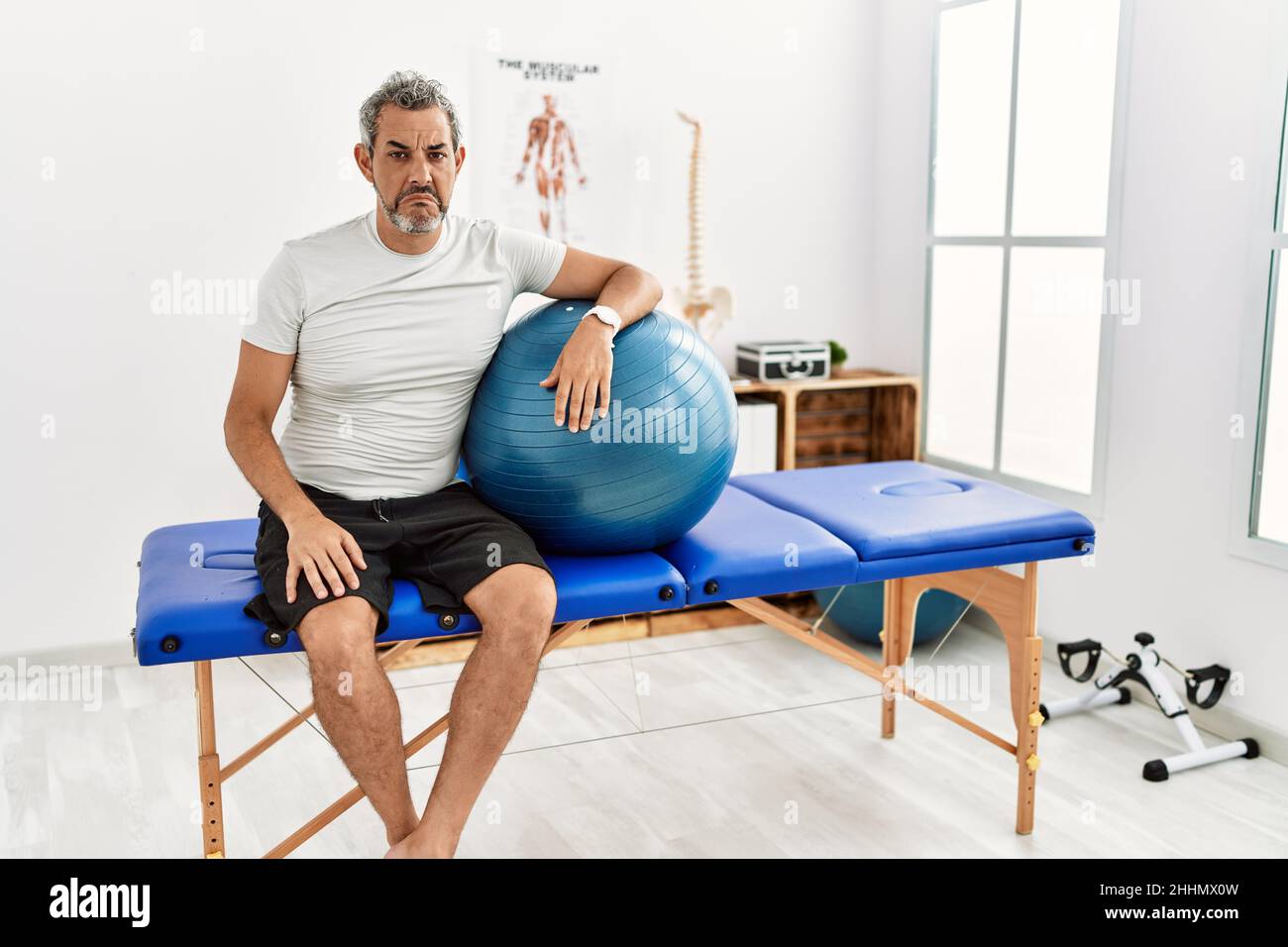 Middle age hispanic man at pain recovery clinic holding pilates ball ...