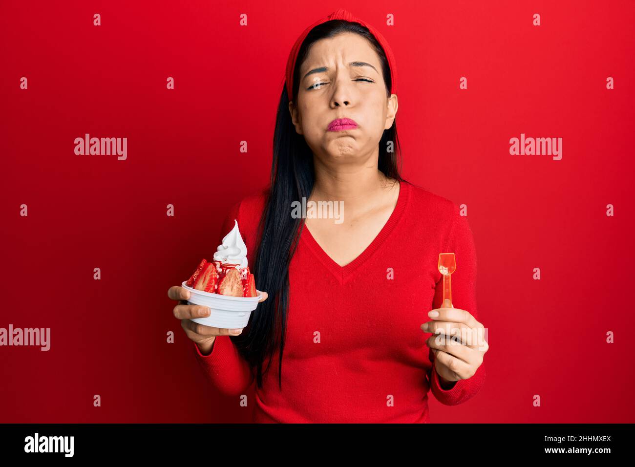 Young latin woman holding ice cream puffing cheeks with funny face. mouth inflated with air ...