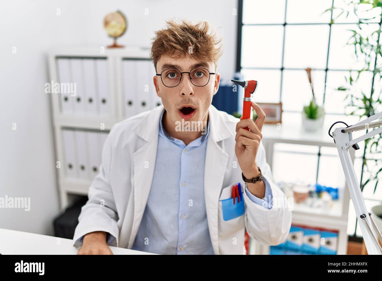 Young caucasian doctor man holding ear otoscope at the clinic scared ...
