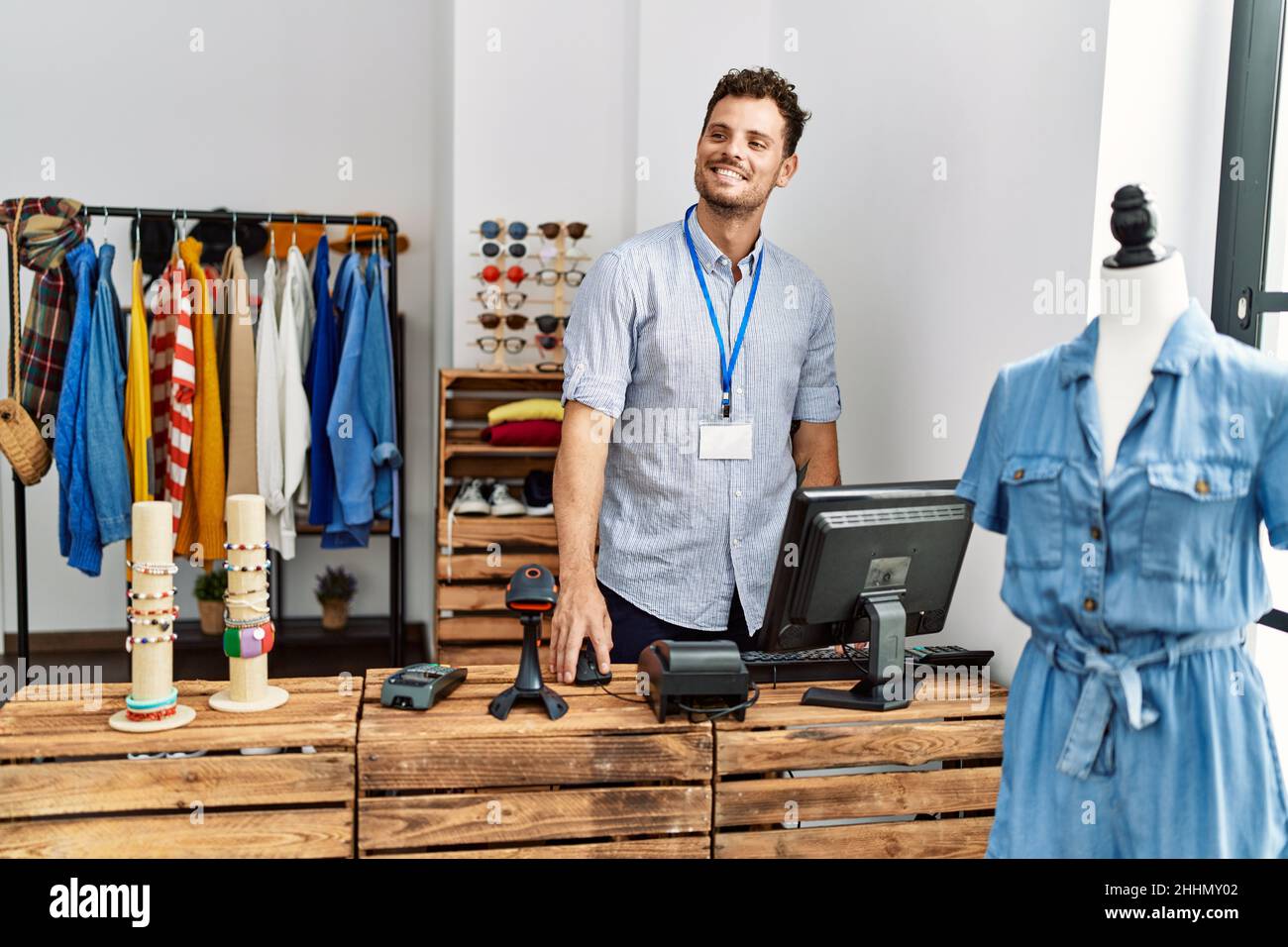 Young hispanic shopkeeper man smiling happy working at clothing store ...