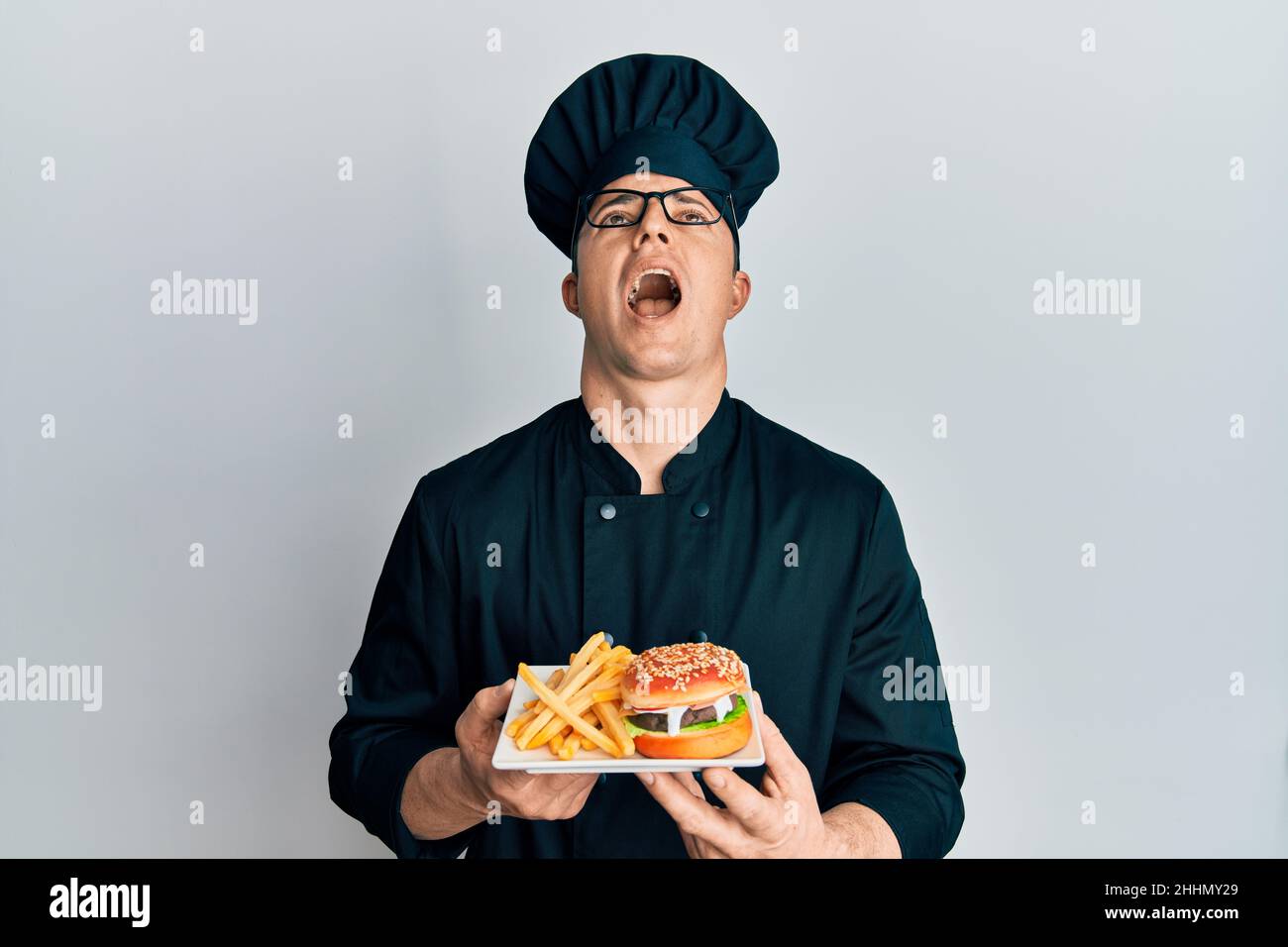 Handsome young man chef holding burger with fries angry and mad ...