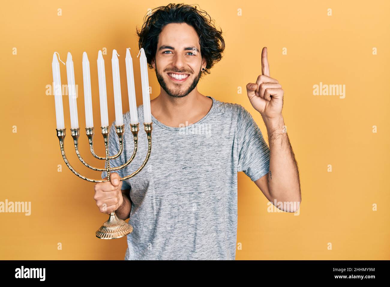 Handsome hispanic man holding menorah hanukkah jewish candle smiling ...