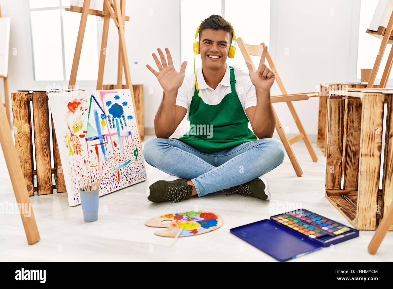 Young hispanic man at art studio showing and pointing up with fingers ...