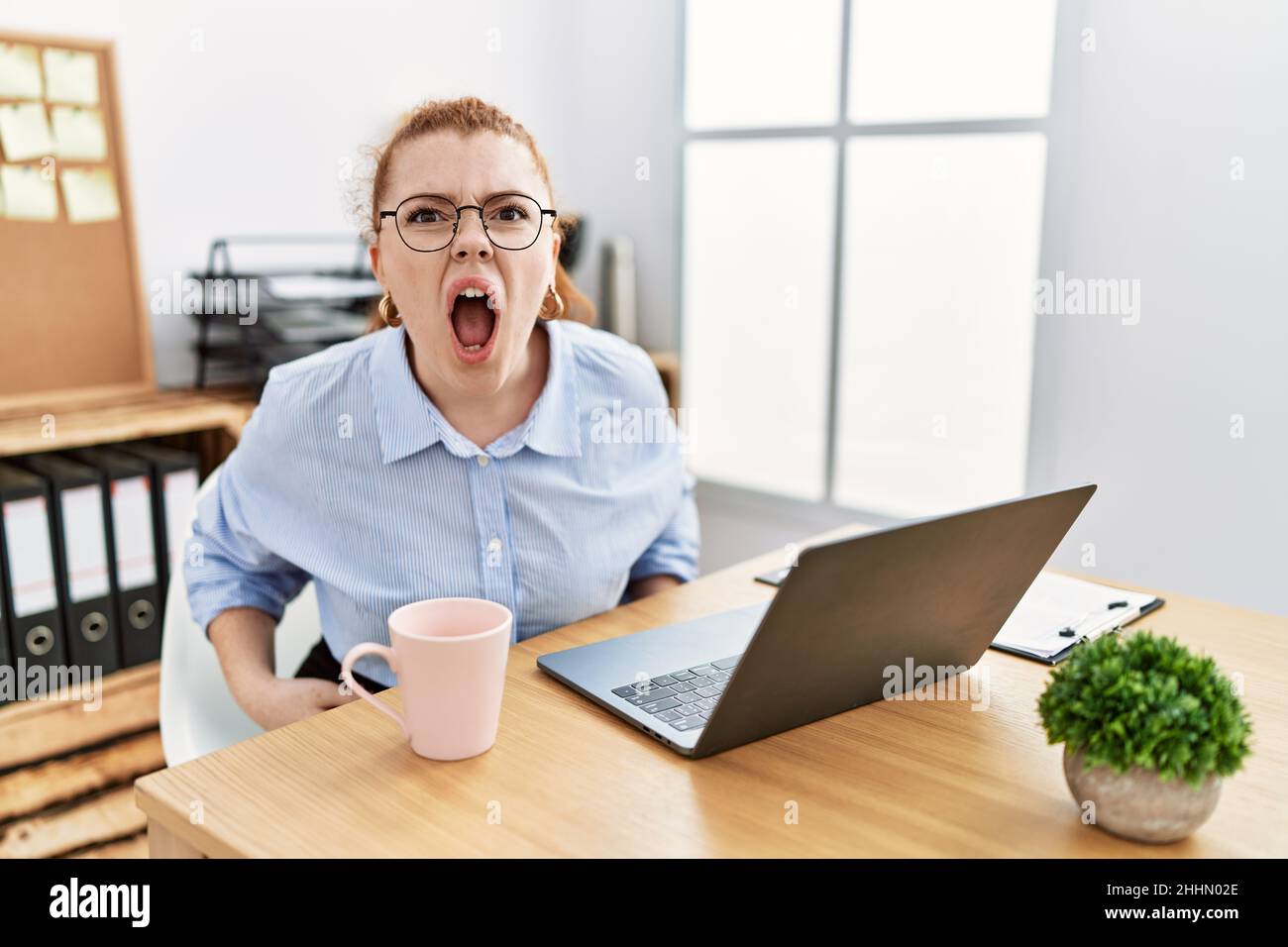 Young redhead woman working at the office using computer laptop angry ...