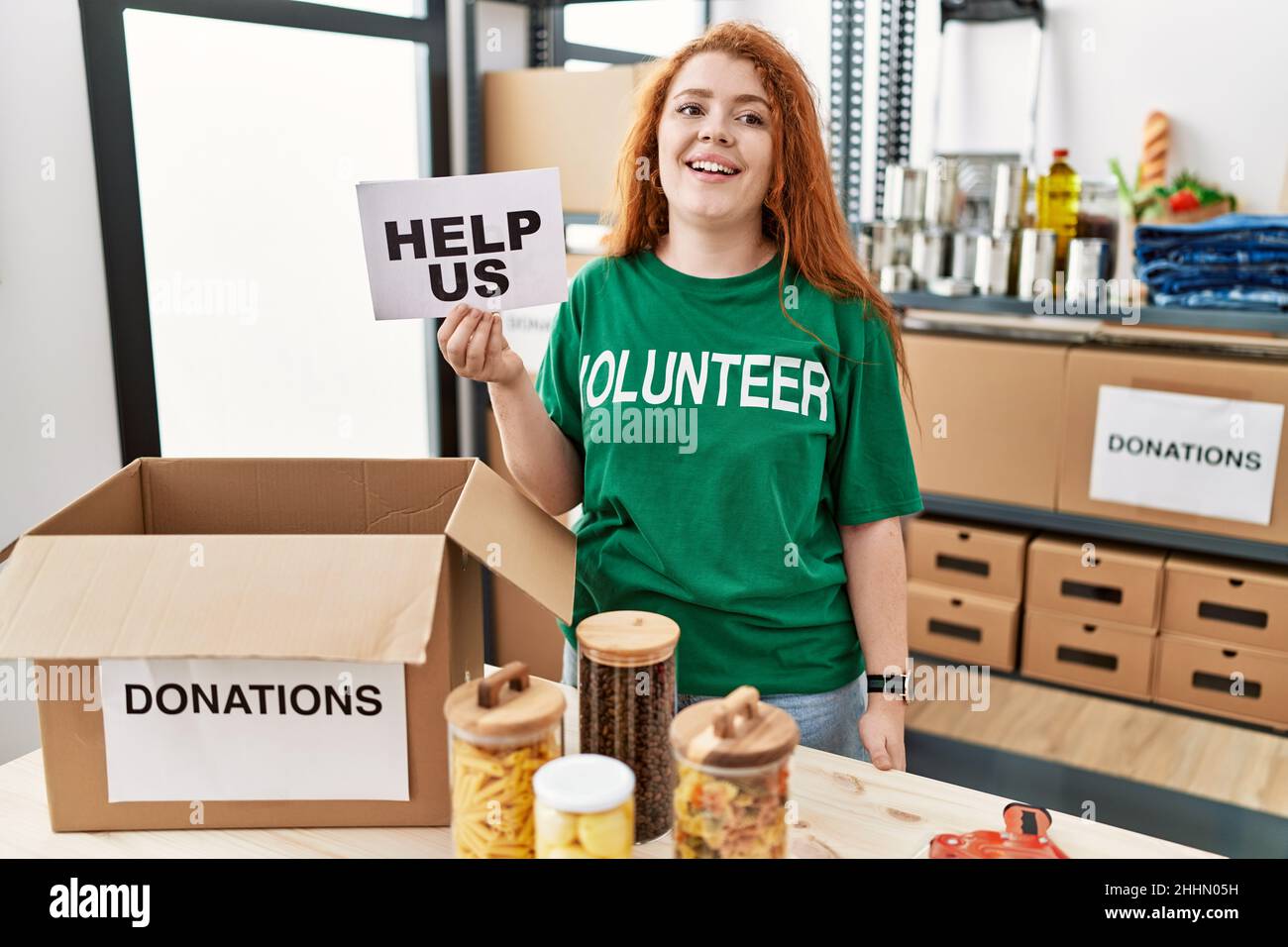 Young redhead woman wearing volunteer t shirt holding help us banner ...