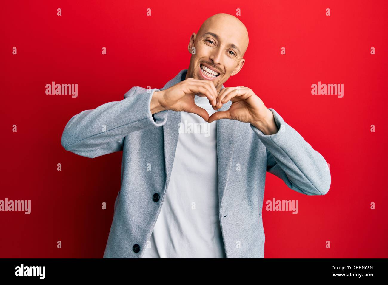 Bald man with beard wearing business jacket smiling in love doing heart ...