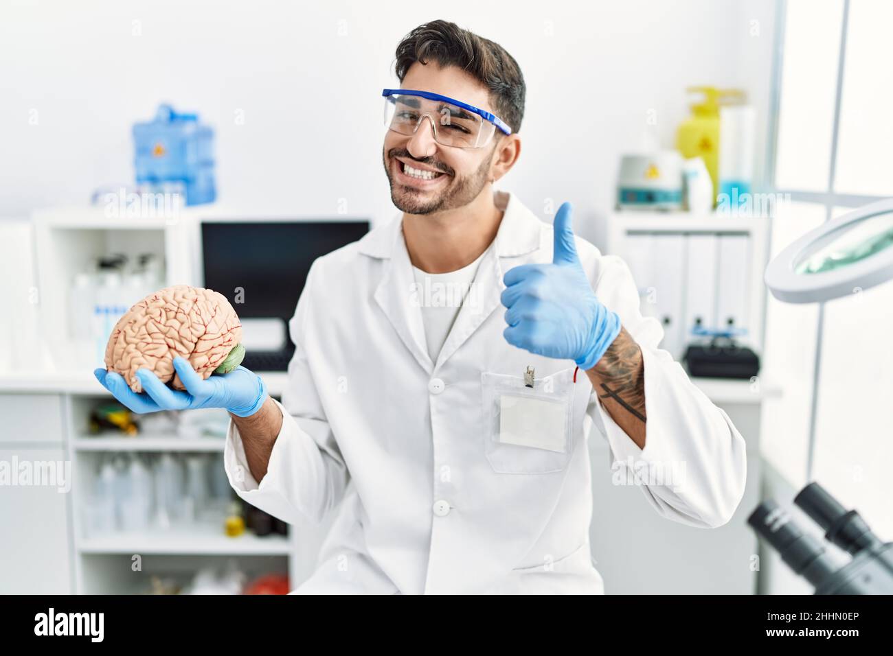 Young hispanic man working at laboratory holding medical brain smiling ...