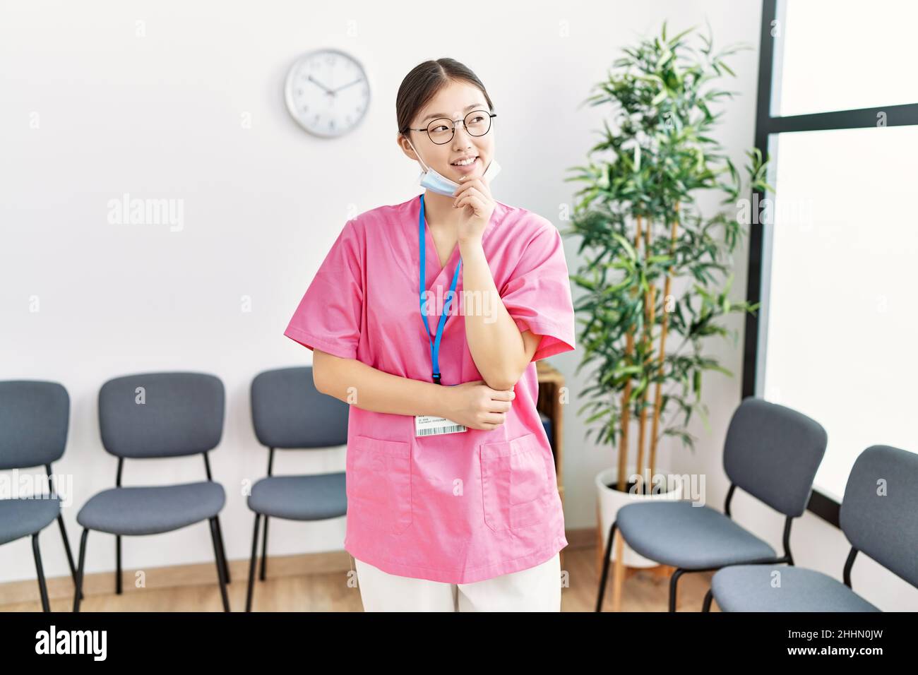 Young asian nurse woman at medical waiting room with hand on chin ...