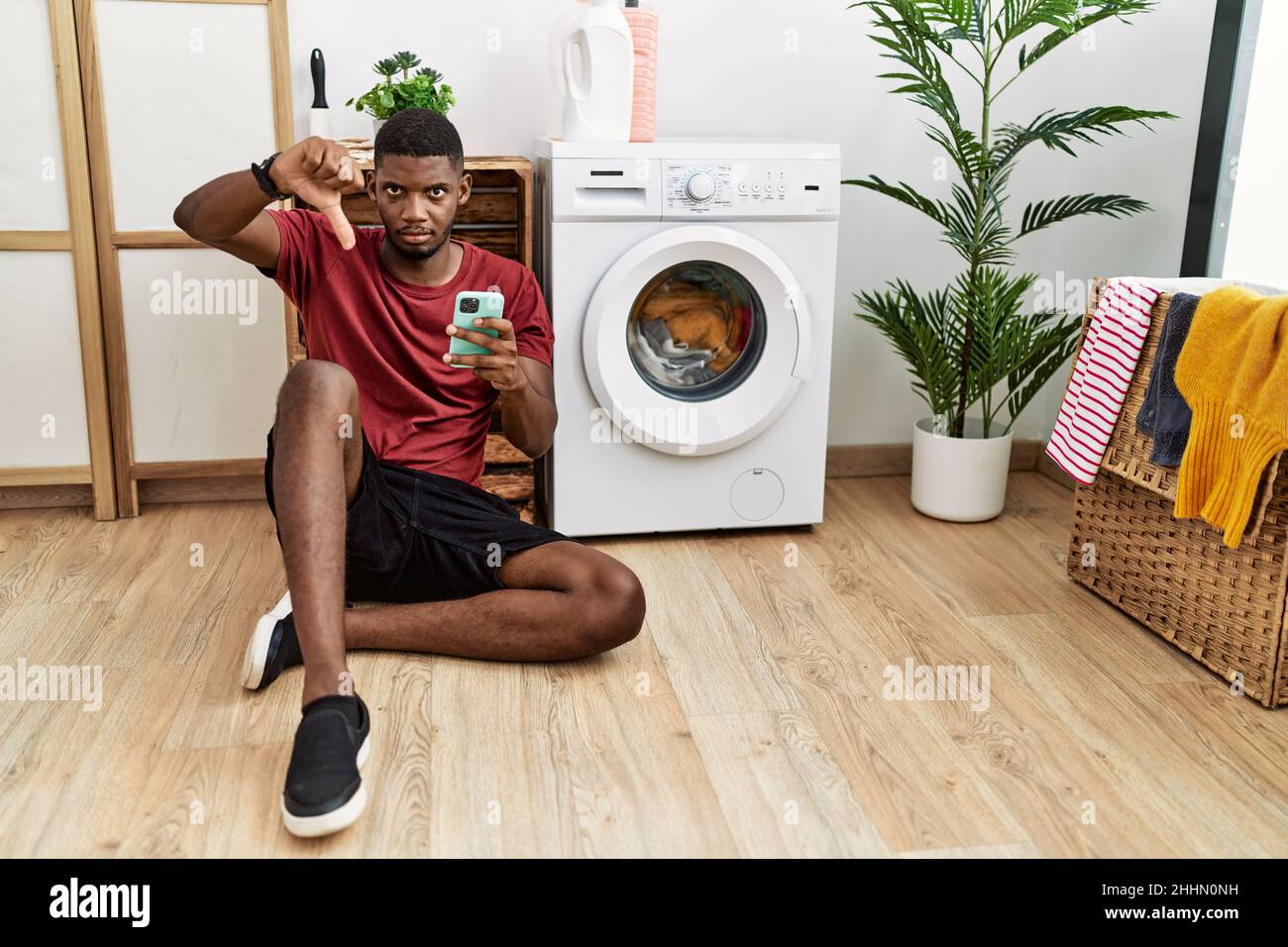 Young african american man using smartphone waiting for washing machine ...