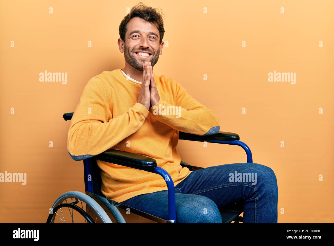 Handsome man with beard sitting on wheelchair praying with hands ...