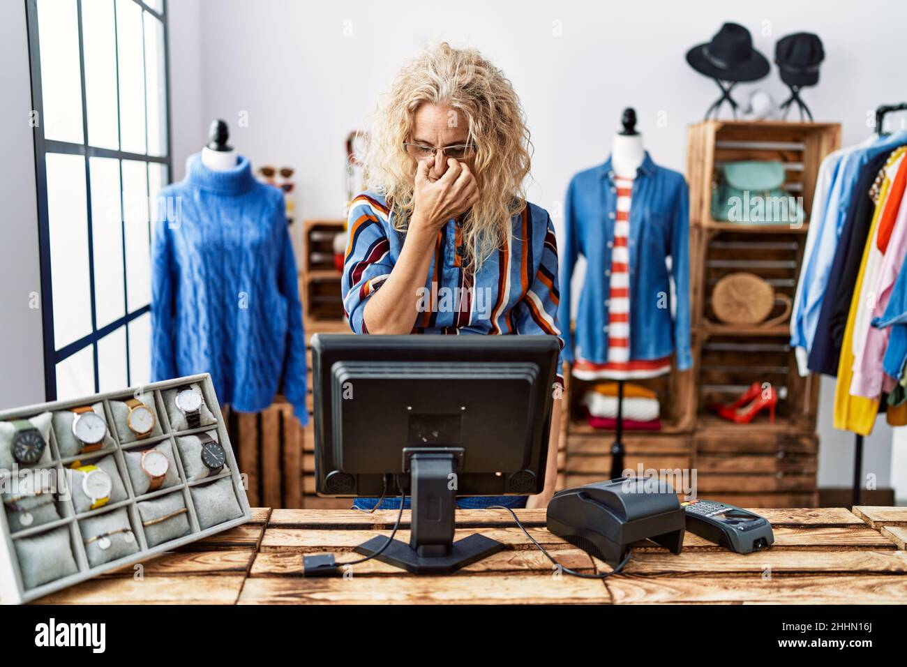 Middle age blonde woman working as manager at retail boutique tired ...