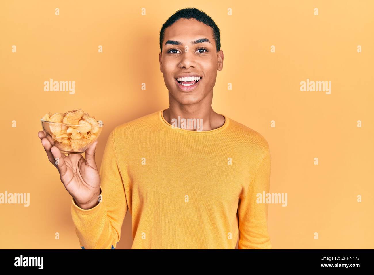 Young african american guy holding potato chip looking positive and ...