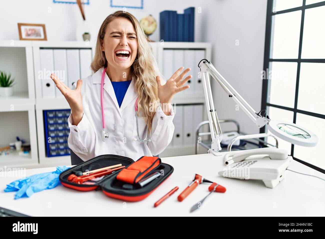 Young beautiful doctor woman with reflex hammer and medical instruments ...