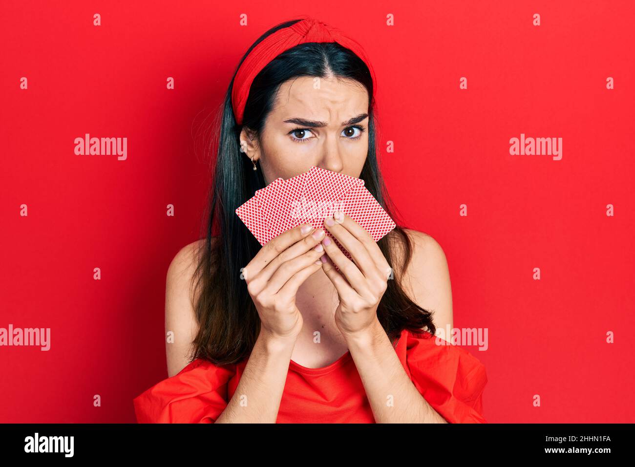 Young brunette woman covering face with cards clueless and confused expression. doubt concept ...