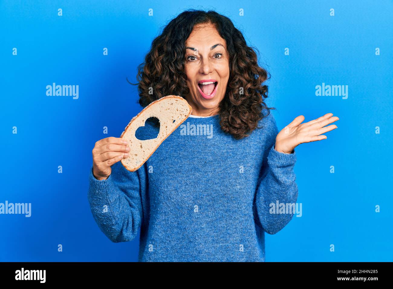 Middle age hispanic woman holding bread loaf with heart shape ...