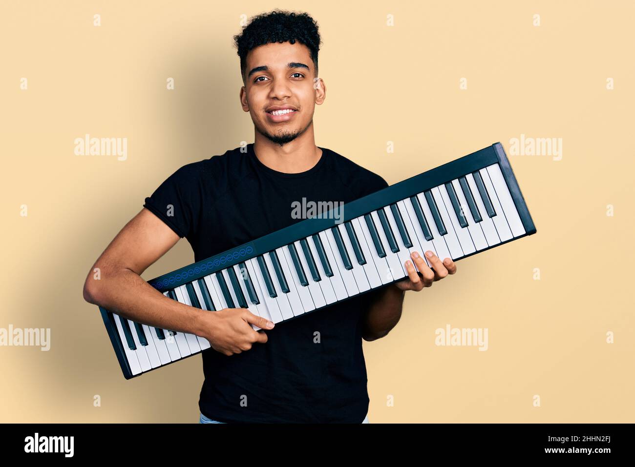 Young african american man holding piano keyboard smiling with a happy ...