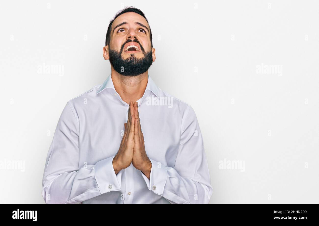 Young man with beard wearing business shirt begging and praying with ...