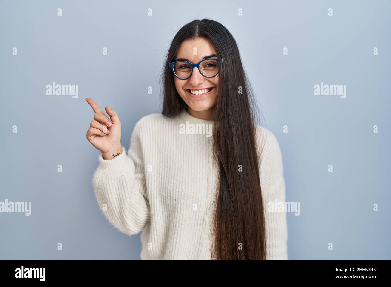 Young hispanic woman wearing casual sweater over blue background with a ...