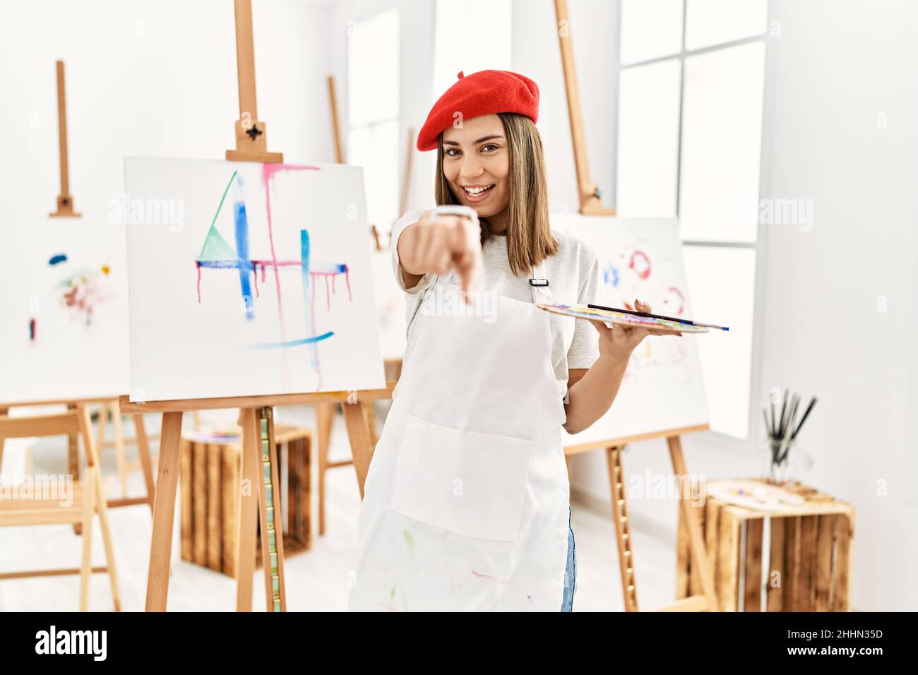 Young artist woman painting on a canvas at art studio pointing to you ...