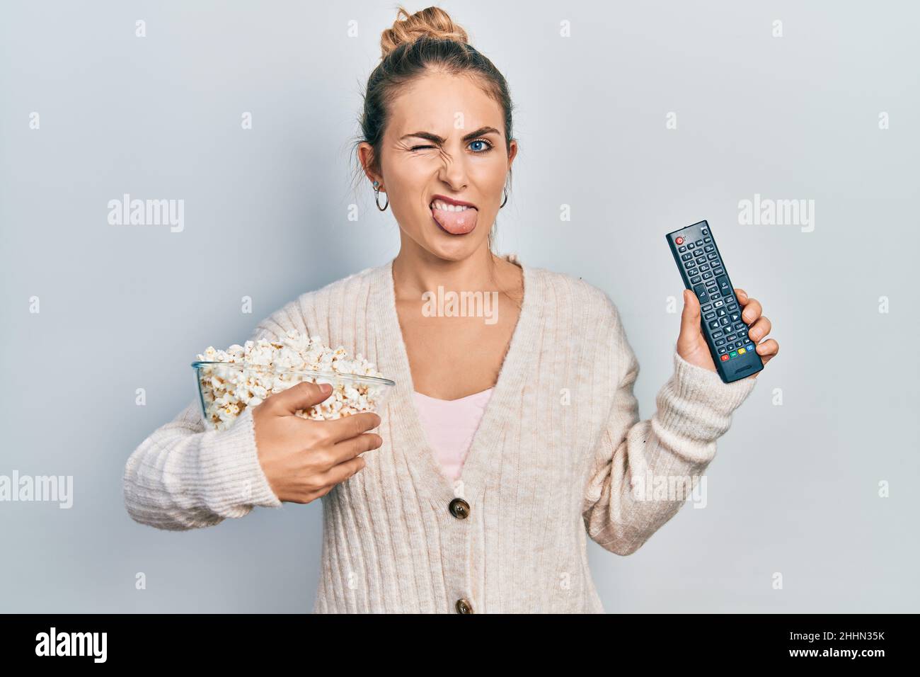 Young caucasian woman eating popcorn using tv control sticking tongue ...