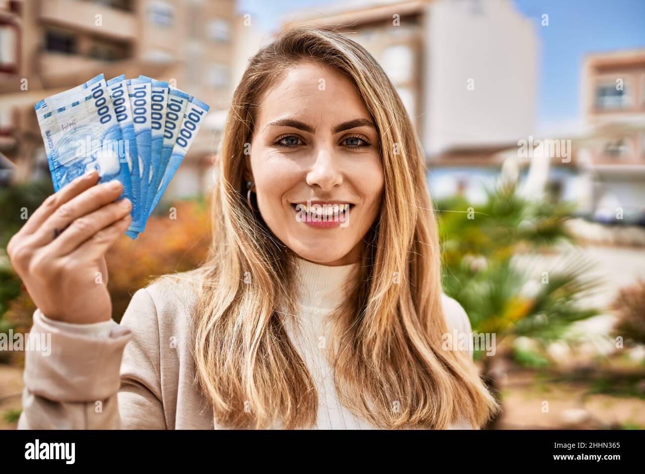 Young blonde woman smiling confident holding chilean pesos banknotes at ...
